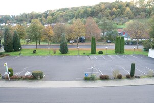 Um estacionamento com vagas demarcadas, alguns carros e vegetação ao redor.