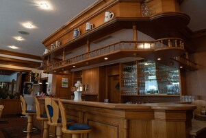 Uma área de bar em madeira com vários níveis, com assentos, um espelho grande e copos em prateleiras.