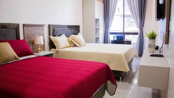 Quarto de hotel com duas camas, uma escrivaninha, televisão e janela com cortinas.