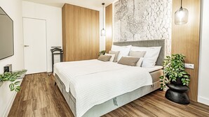 Quarto moderno com uma cama grande, painéis de madeira, luminária pendente e um vaso com planta.