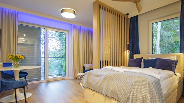 Quarto moderno com uma cama grande, um ventilador de teto e vista para árvores pelas janelas.