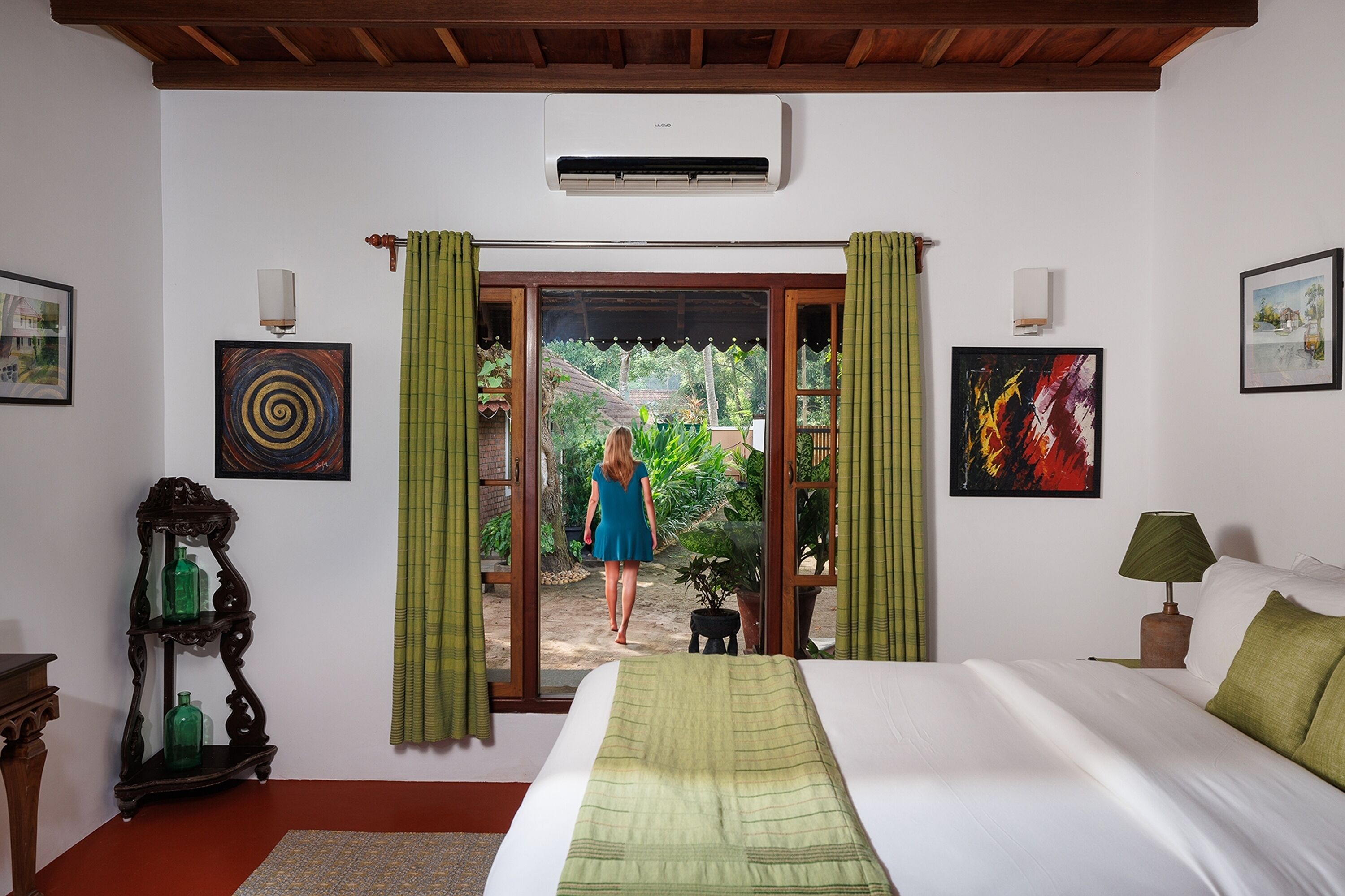 Quarto com cama grande, janela com cortinas, ar condicionado na parede e obras de arte nas paredes.