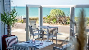 Um terraço com mesa e cadeiras, um vaso de planta e vista para o mar.