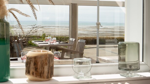 Uma área de refeições com vista para o mar, uma mesa com cadeiras e um guarda-sol listrado.