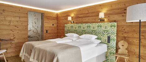 Quarto de madeira com cama, duas luminárias na parede, uma mesinha e uma cadeira.