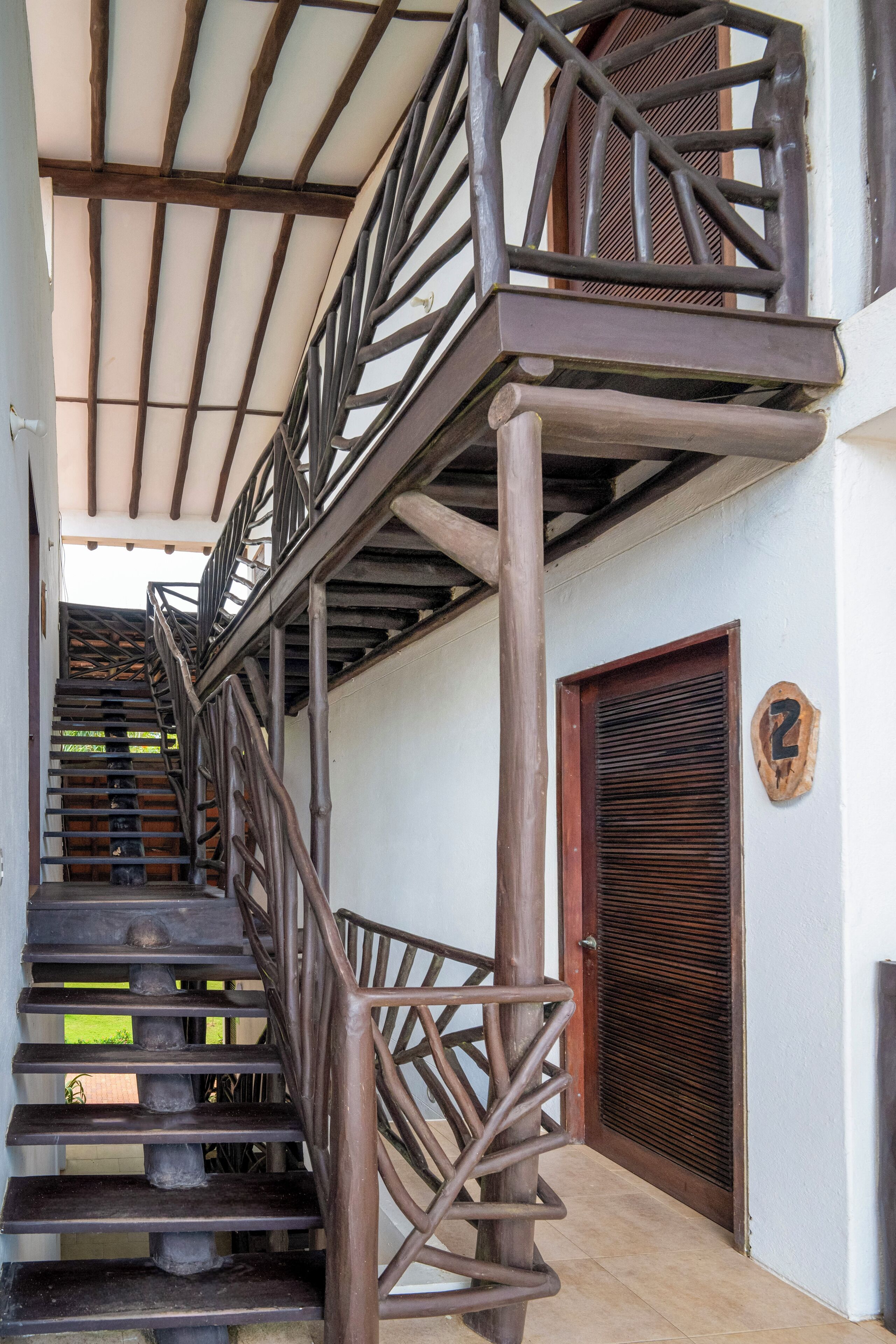 Uma escada de madeira com corrimão de metal que leva a uma porta com a placa de número '2'.