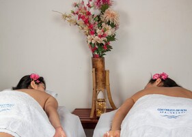 Duas salas de tratamento de spa com toalhas brancas, uma cadeira de madeira e um vaso de flores.
