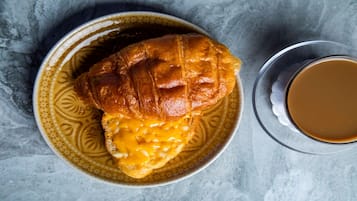Sanduíche de croissant com queijo derretido sobre um prato estampado, acompanhado de uma xícara de café.