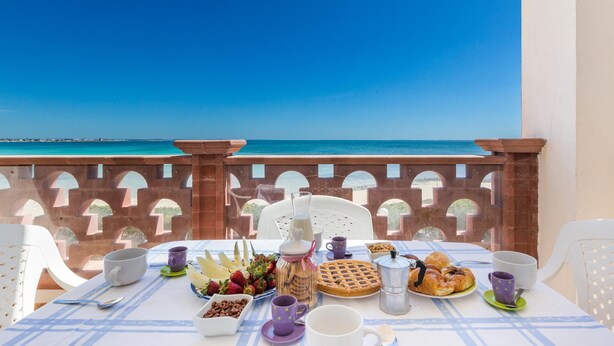 Mesa posta com itens de café da manhã e vista para o mar.