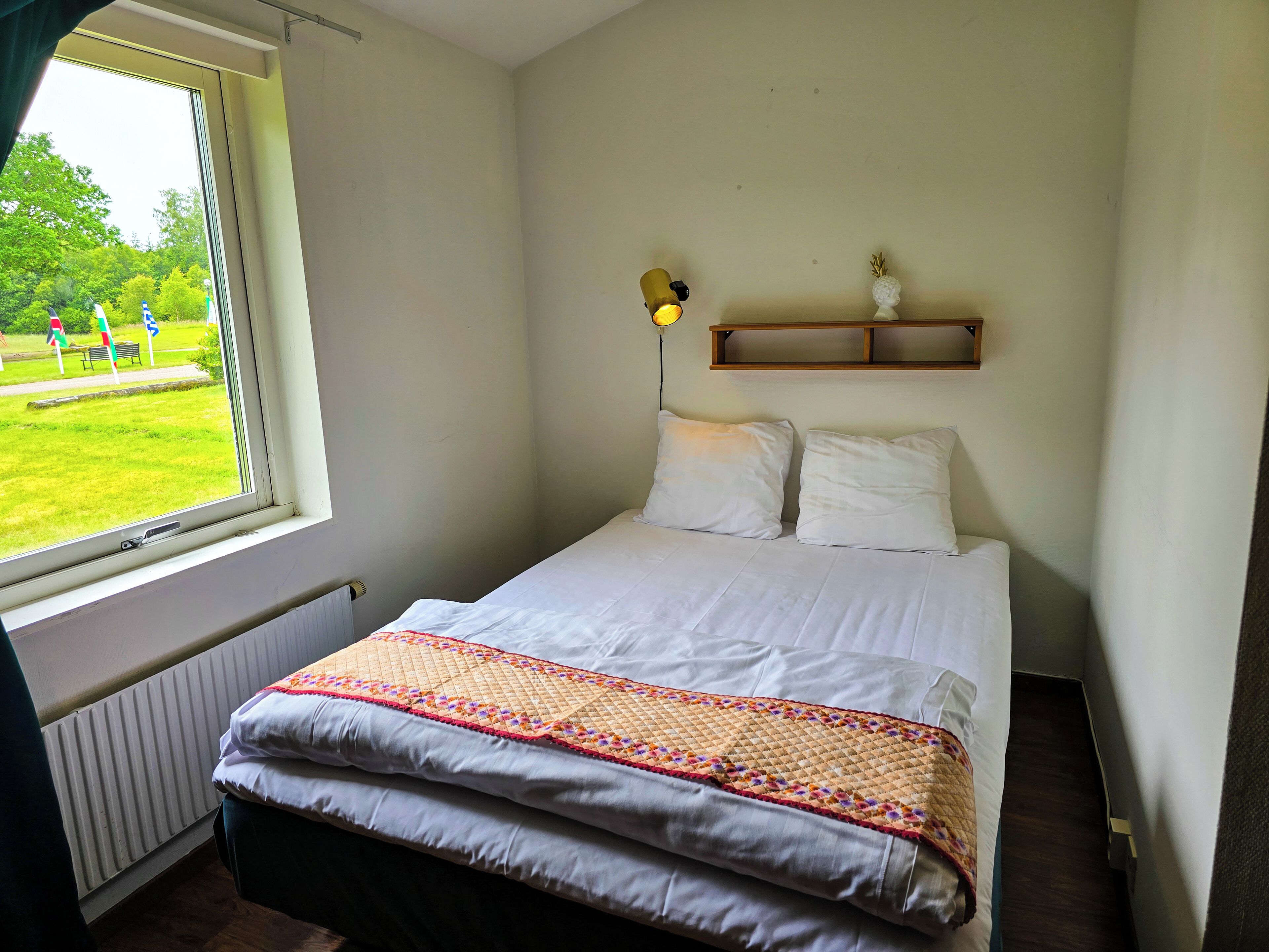Quarto com cama, janela, radiador e mesa de cabeceira.