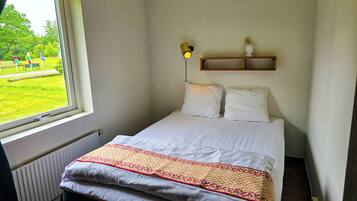 Quarto com cama, janela, radiador e mesa de cabeceira.