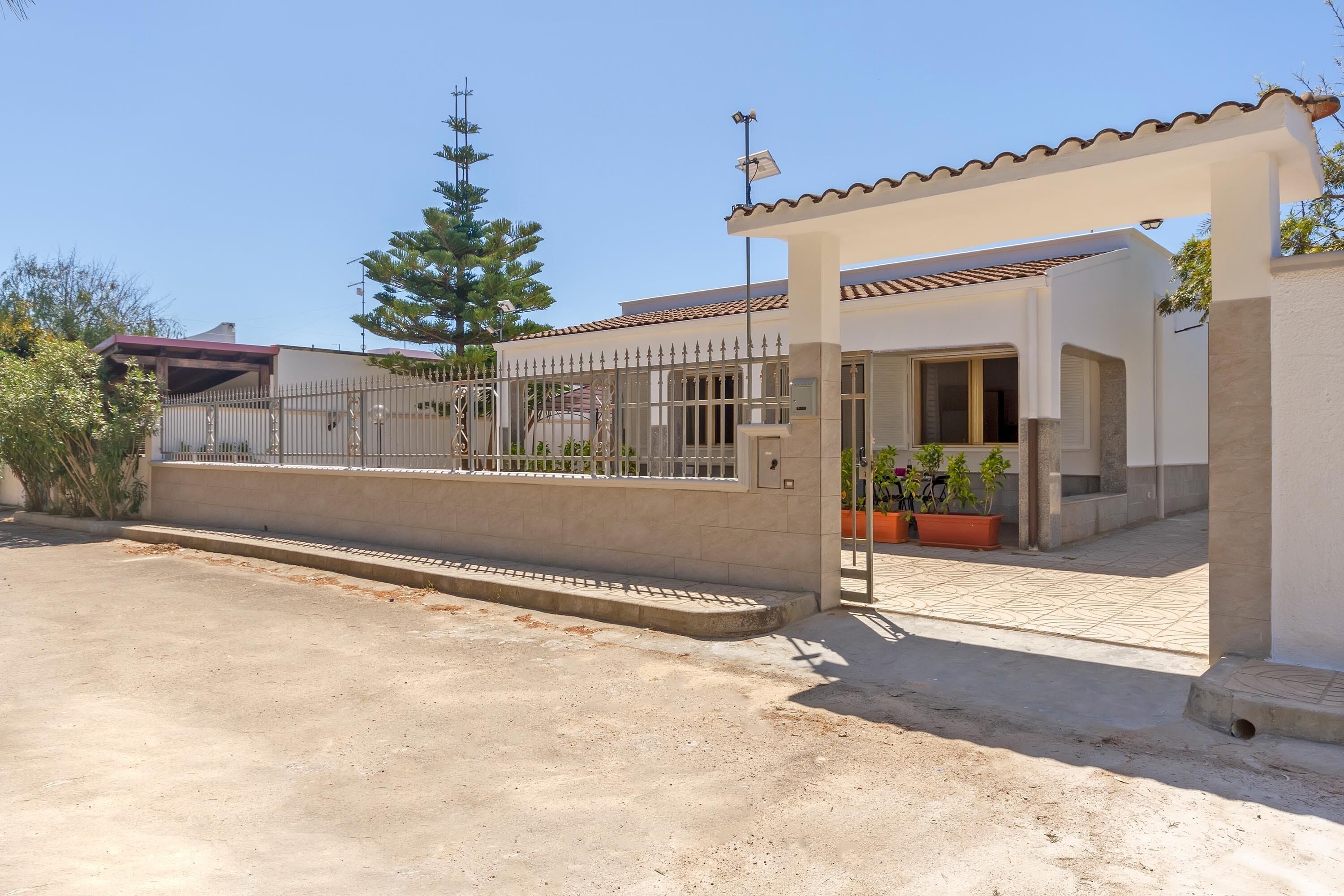 Um condomínio residencial com portão, uma varanda coberta, entrada de veículos em concreto e cerca de metal.
