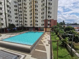 Piscina rodeada por um deck revestido com azulejos, com vista para um edifício alto ao fundo.