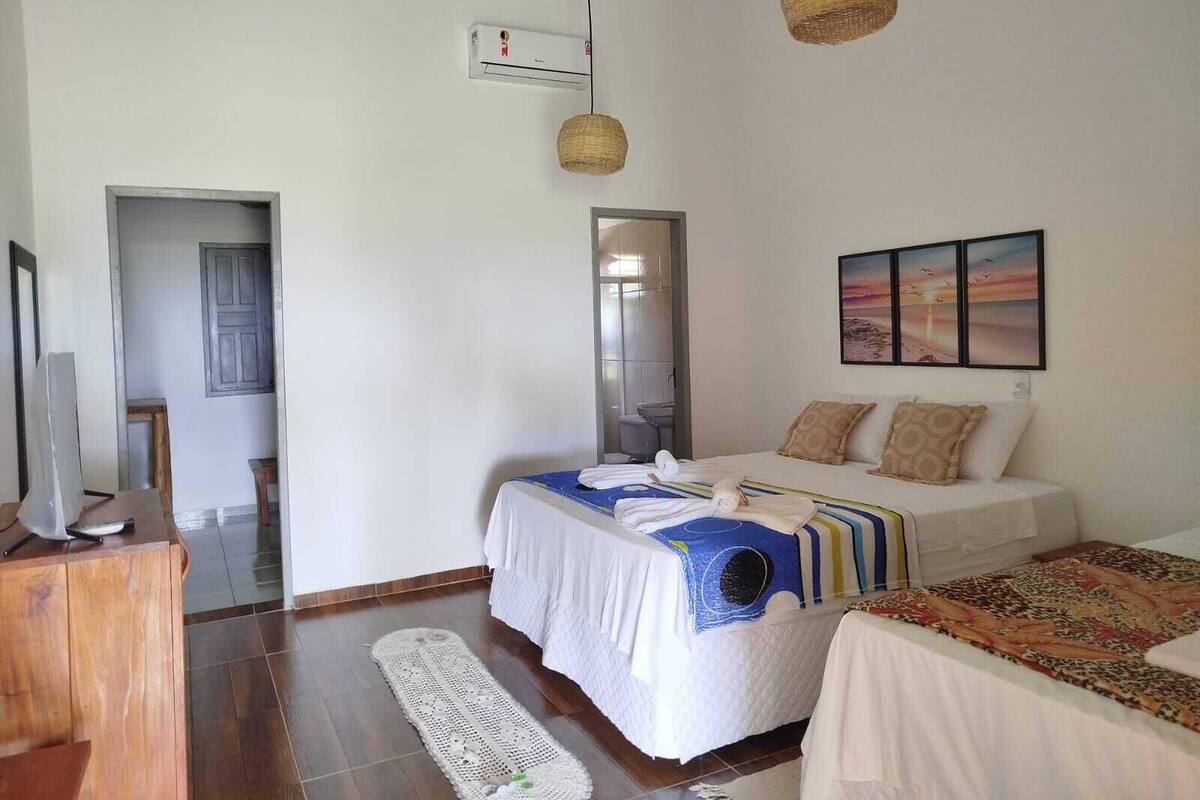 Quarto com cama, mesa de cabeceira, espelho, ar condicionado fixado na parede e um quadro.