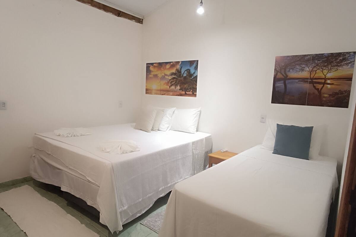 Quarto com duas camas, uma mesa pequena e duas pinturas nas paredes.
