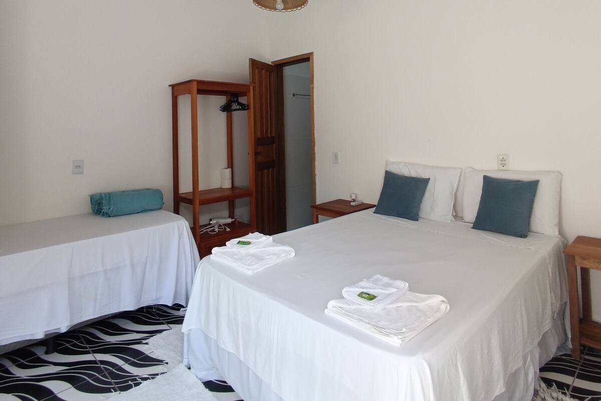 Quarto com duas camas, uma estante de madeira, uma luminária pendente e um tapete estampado.