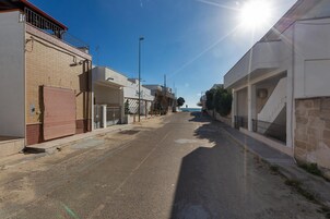 Rua tranquila com edifícios em ambos os lados, céu claro e sol brilhando.