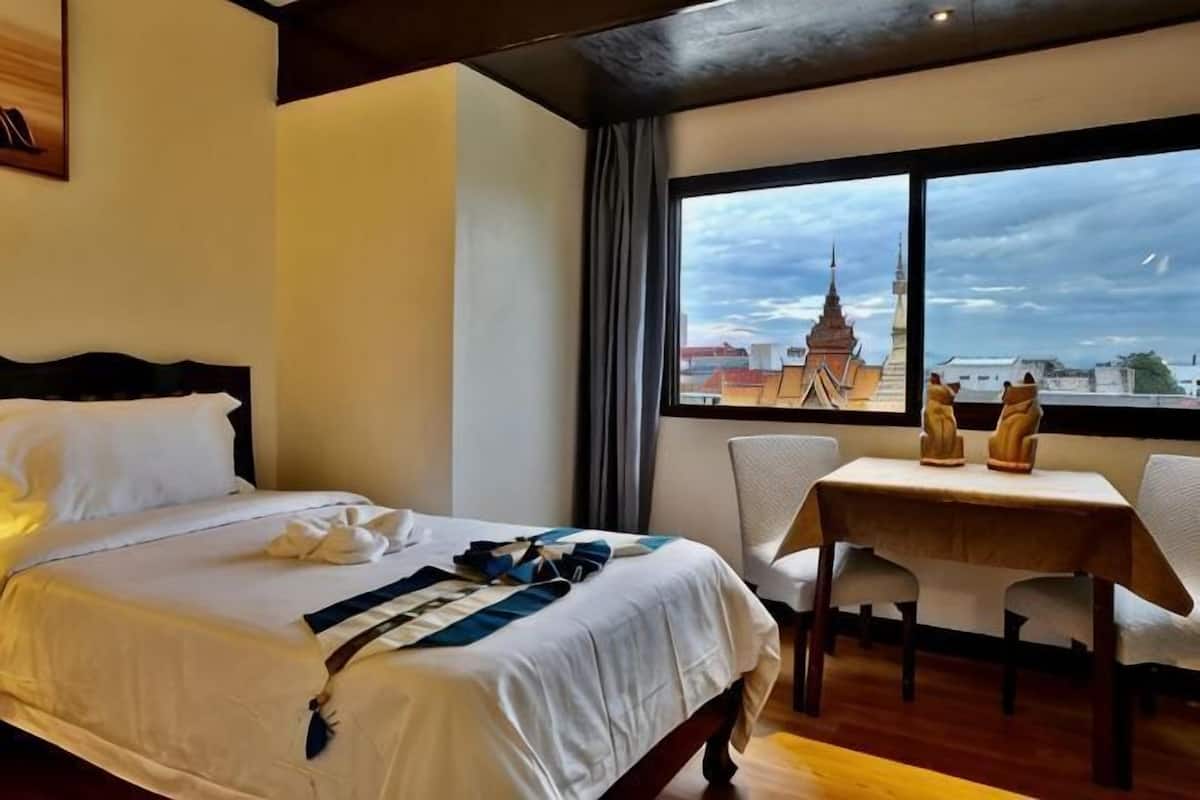 Quarto de hotel com cama, mesa e cadeiras, e janela com vista para a cidade.