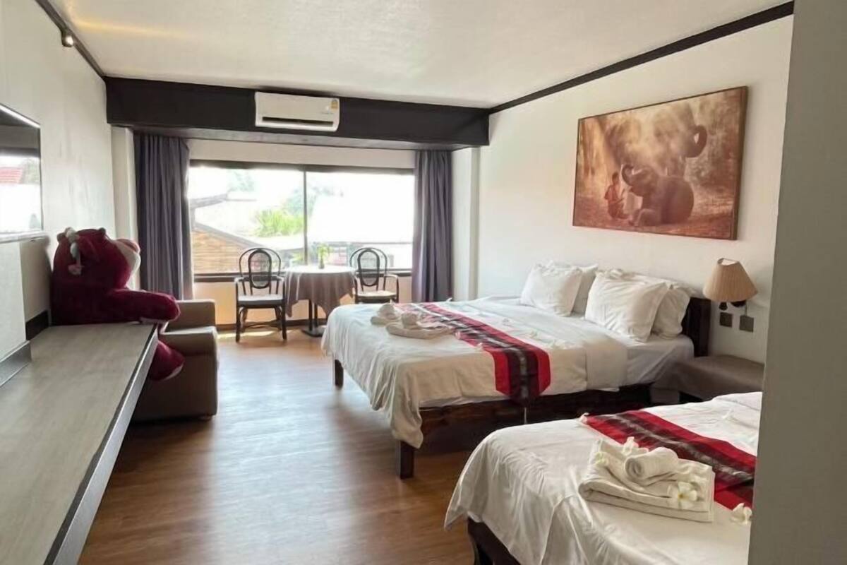 Quarto de hotel com duas camas, uma mesa, uma cadeira e uma janela grande.