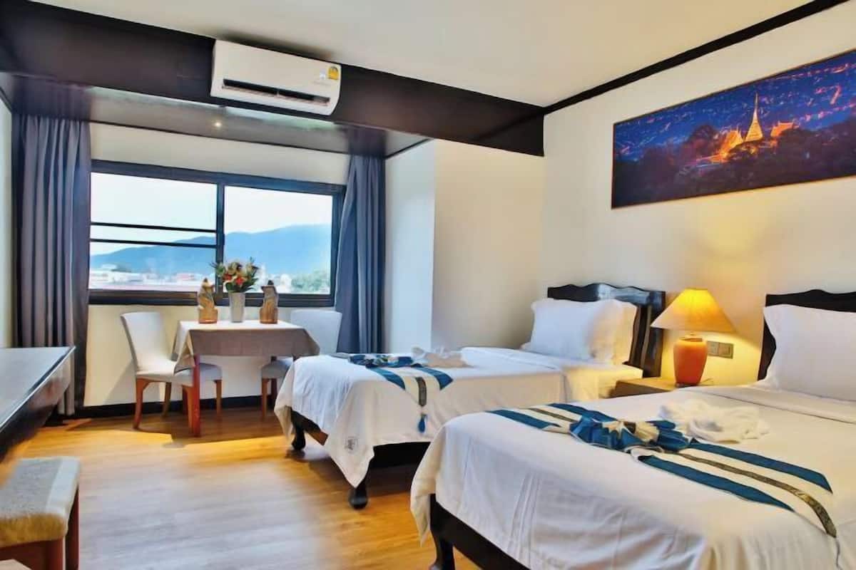 Quarto de hotel com duas camas, uma escrivaninha, uma cadeira e uma janela ampla com vista para as montanhas.