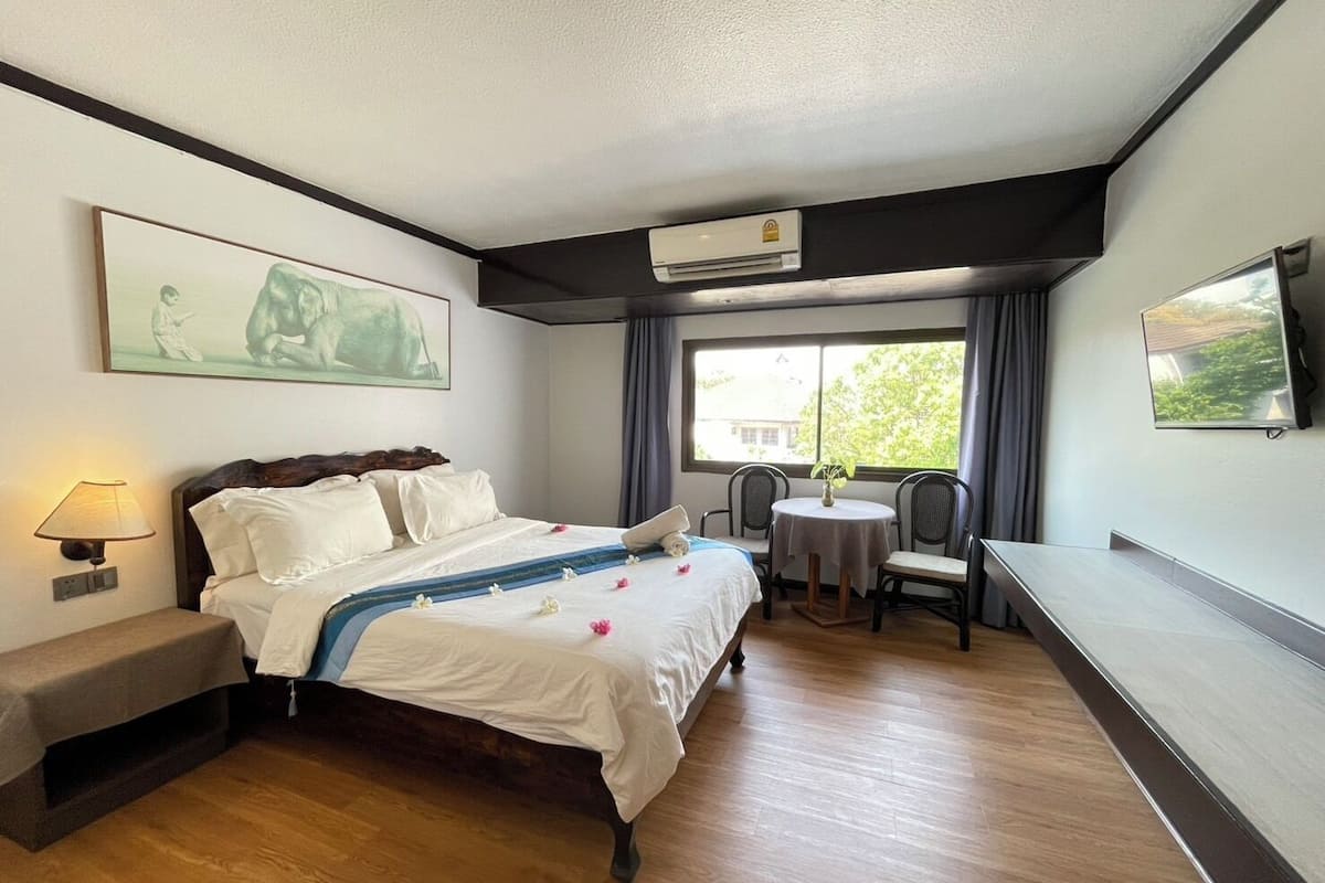 Quarto de hotel com cama, mesa de cabeceira, luminária, ar condicionado, janela com cortinas e televisão.