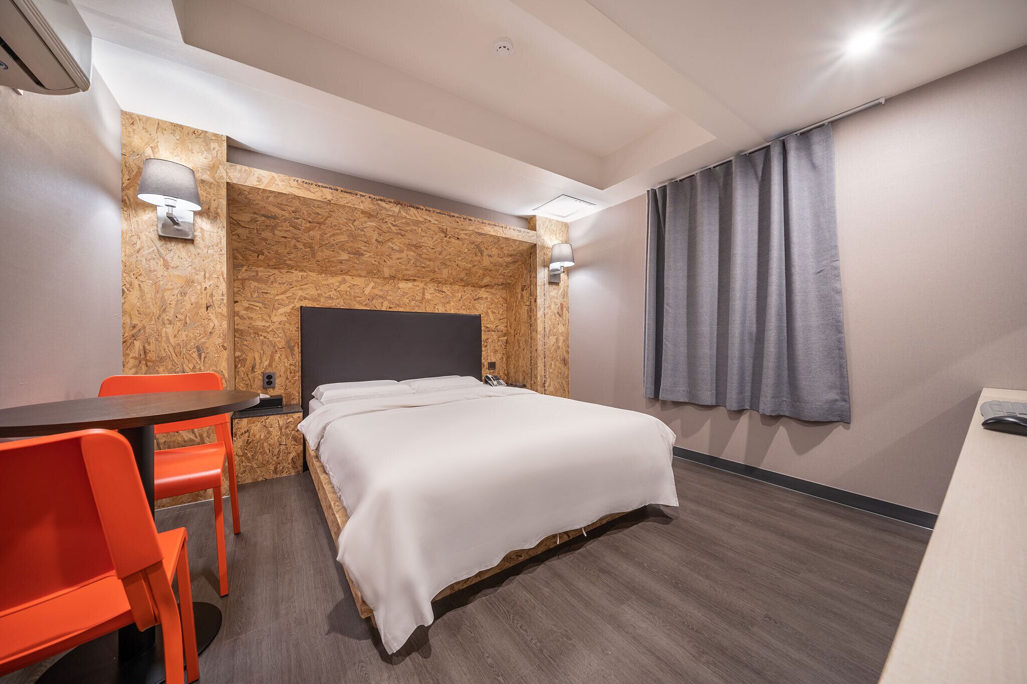 Quarto de hotel com uma cama, uma escrivaninha e duas cadeiras.