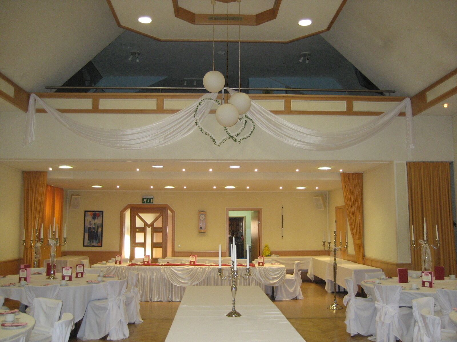 Uma sala de banquetes com mesas preparadas para eventos, lustres e teto alto com vigas de madeira.
