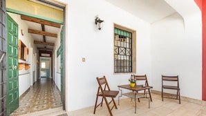Um corredor com chão de azulejos, molduras de porta em madeira e uma pequena mesa com cadeiras.