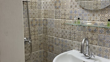 Casa de banho com chuveiro, lavatório e paredes em azulejo.