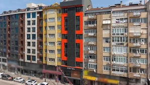 Hotel de vários andares com varandas, entrada central e estacionamento com carros.