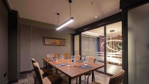 Uma sala de conferências com uma mesa comprida, cadeiras, garrafas de água e um quadro na parede.