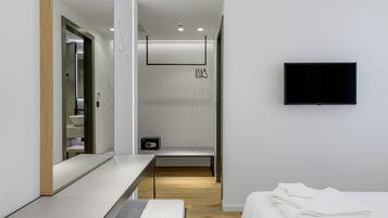 Quarto de hotel moderno com um espelho grande, uma televisão de tela plana, um banco e uma cama bem arrumada.