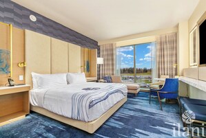 Quarto de hotel com cama grande, escrivaninha, cadeira e vista para o exterior.
