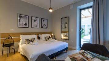 Quarto de hotel com cama, uma cadeira, mesa com revistas e janela com cortinas.