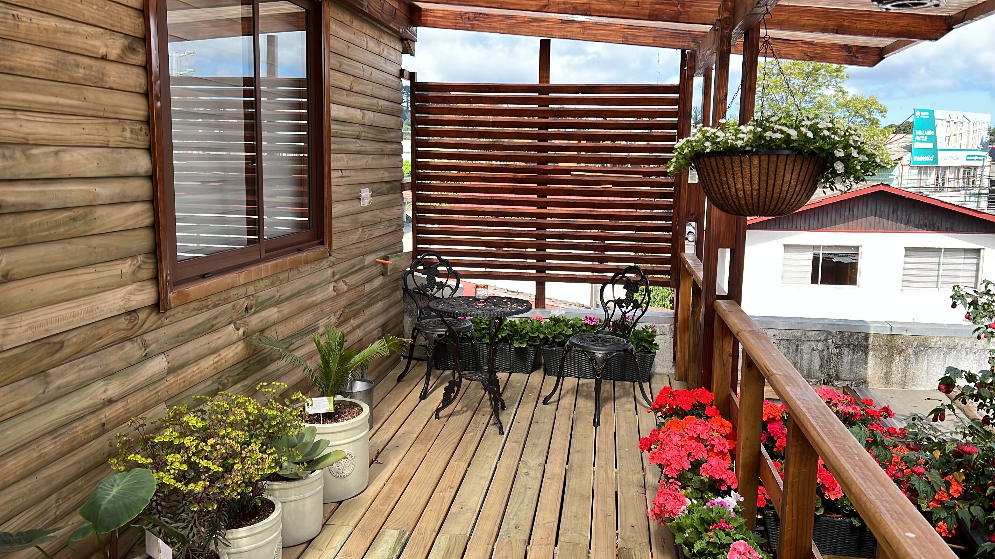 Varanda de madeira com grade de madeira, plantas em vasos e mobiliário de exterior.