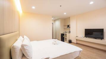 Quarto de hotel com uma cama, televisão fixada na parede e pequena área de cozinha.