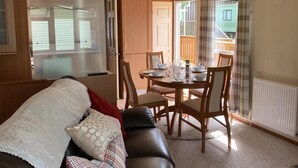 Uma sala de estar aconchegante com um sofá, uma mesa de jantar posta para quatro pessoas e vista para uma casa móvel verde pela janela.
