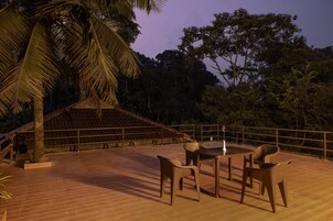 Terraço ao ar livre com mesa e cadeiras, cercado por palmeiras e vista para a floresta.