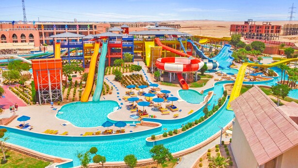 Um parque aquático com várias piscinas e toboáguas, rodeado por edifícios e paisagem desértica.