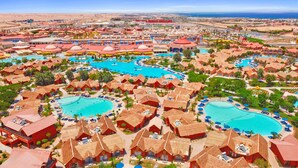 Um resort com várias piscinas, chalés com telhados de palha e vista para o oceano.