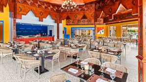 Um restaurante espaçoso com tetos altos e detalhes em madeira elaborados, com várias áreas de refeição, cadeiras de vime e mesas.