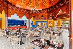 Um restaurante espaçoso com tetos altos e detalhes em madeira elaborados, com várias áreas de refeição, cadeiras de vime e mesas.
