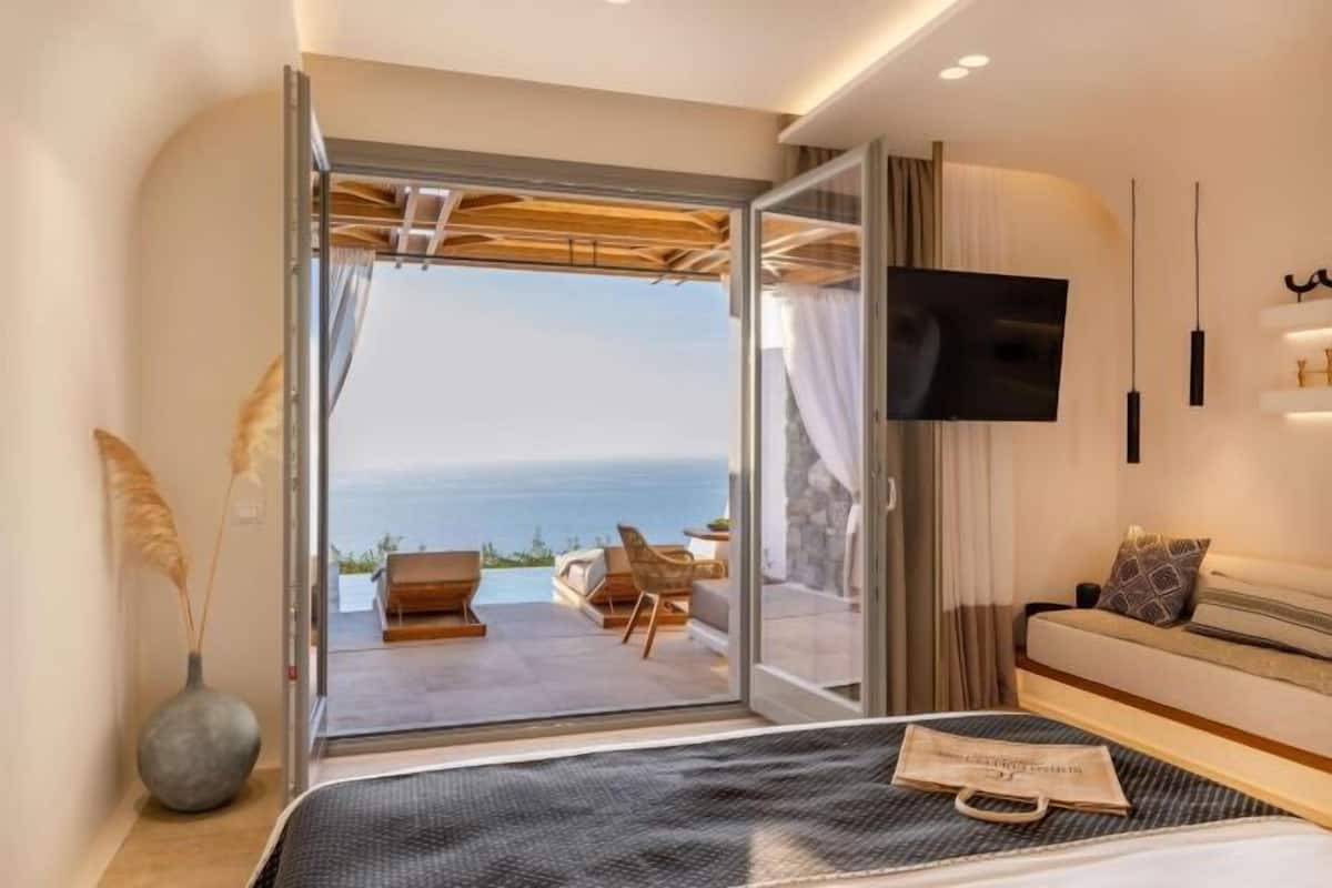 Quarto com cama, televisão, sofá e varanda com vista para o mar.