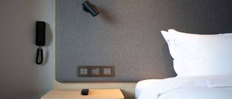 Quarto de hotel com uma cama, mesa de cabeceira, telefone e painel de controle na cabeceira.