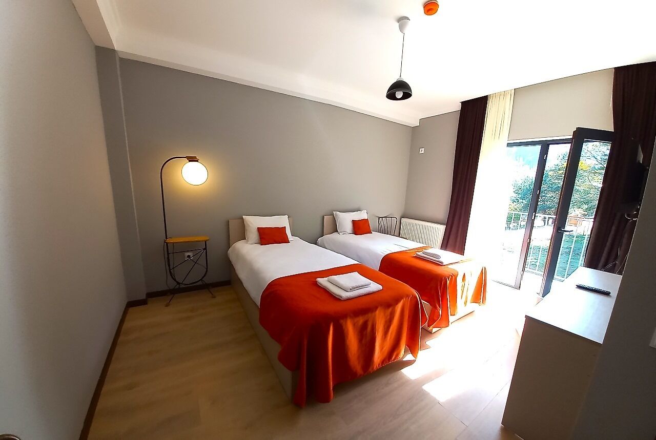 Quarto de hotel com duas camas, uma escrivaninha, uma cadeira, um abajur e uma janela com cortinas.
