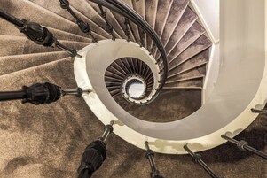 Uma escadaria em espiral com um patamar circular no centro e corrimãos em ambos os lados.