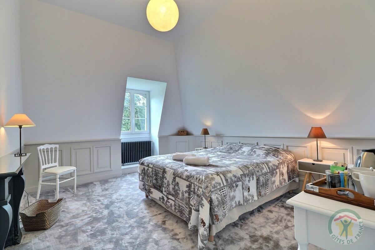 Quarto com cama, duas mesas de cabeceira, uma cadeira, janela e radiador.