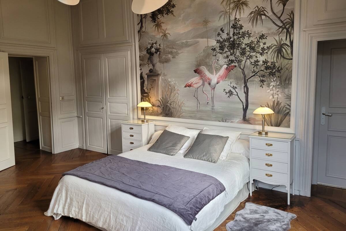 Quarto com cama grande, duas mesas de cabeceira, um mural na parede e piso de madeira.