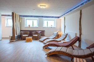 Uma sala de sol com espreguiçadeiras de madeira, cadeiras de vime e uma janela grande.