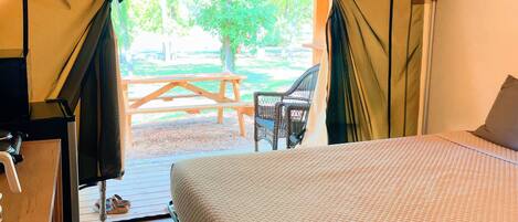 Alojamento tipo tenda com cama, mesa e vista para área externa com mesa e cadeiras de piquenique.